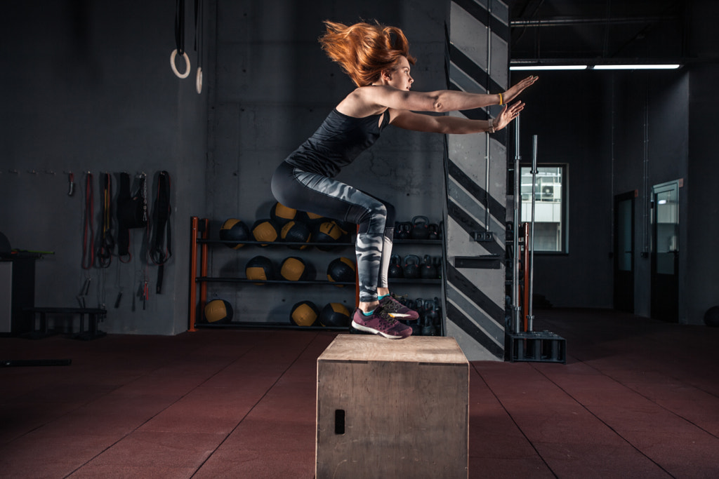 Sporty girl jumping over some boxes in a cross-training gym by Oleksandr Boiko / 500px