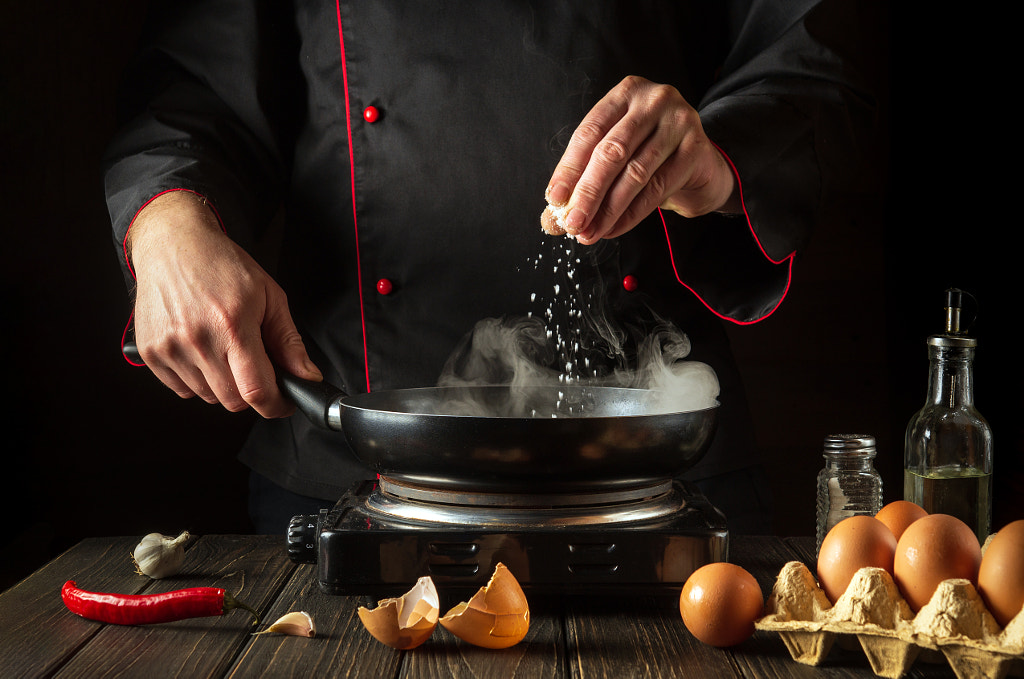 The chef adds salt while cooking eggs in pan by Vitaliy Borkovskiy / 500px