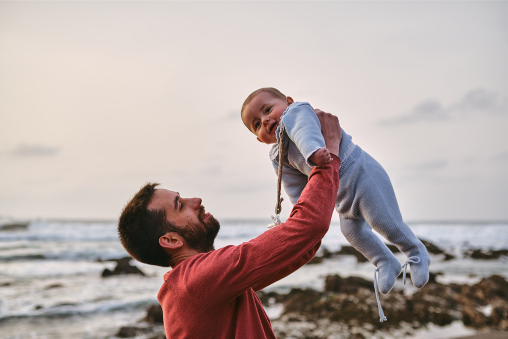 Young single father lifting his baby and playing with him on the beach ...