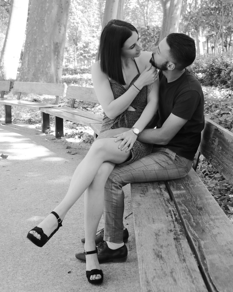 Young couple sitting on bench at park by Bruno Vilbé / 500px