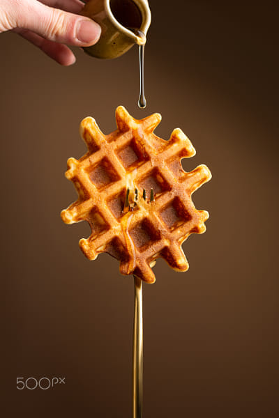 Ruddy waffle on a golden fork with a flowing drop of sweet syrup by ...