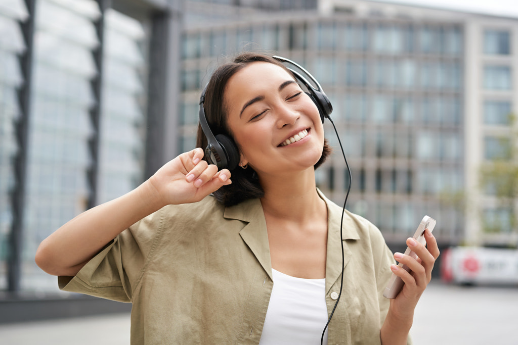 Happy girl dances on street and listens music in wireless headphones by Mix and Match Studio / 500px