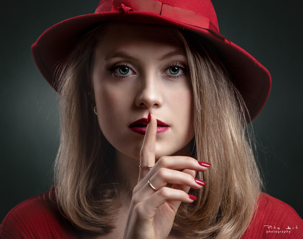 Portrait of young woman wearing red hat against black background by ...
