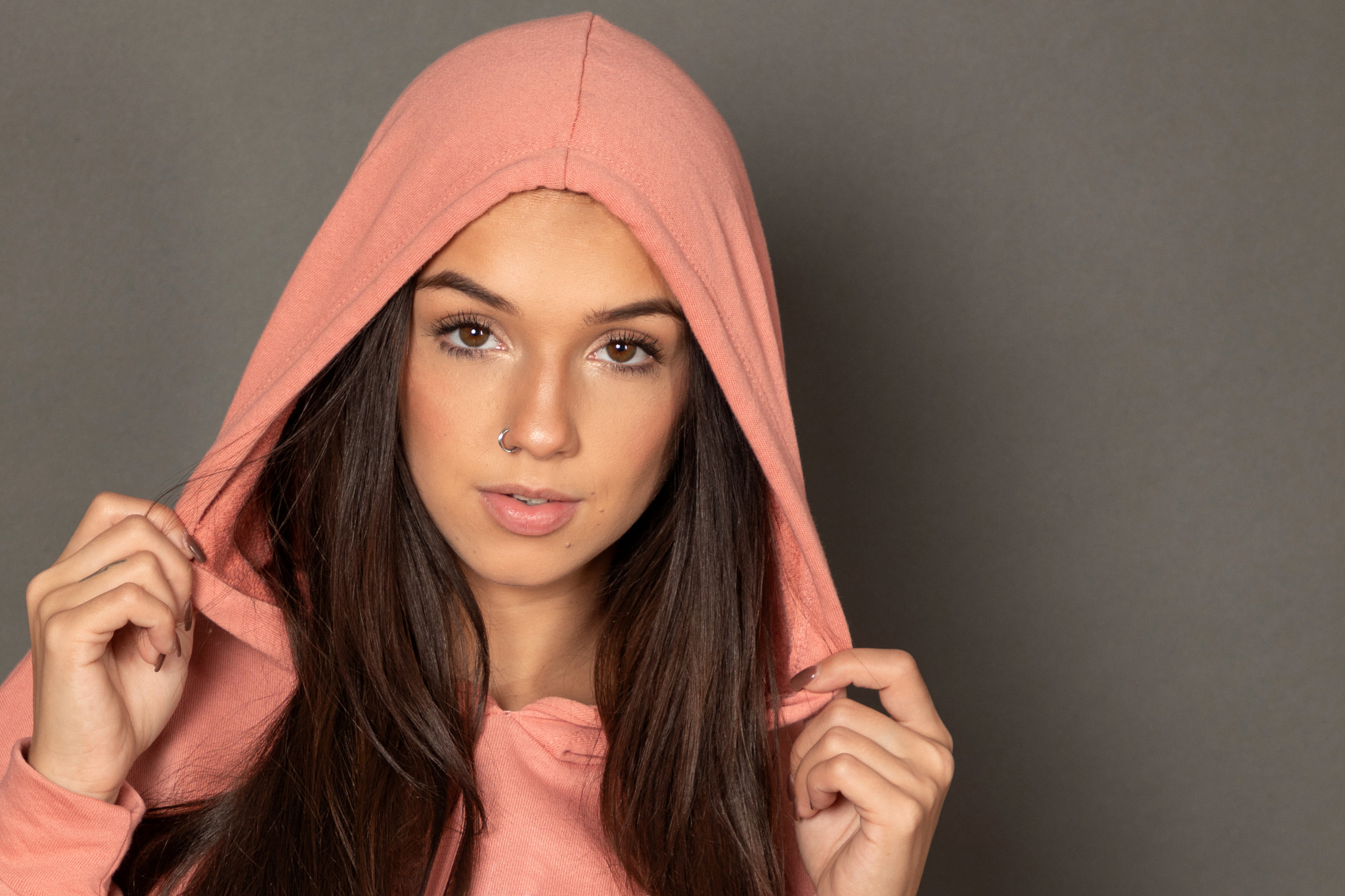 Portrait of young woman wearing hood clothing against gray background ...