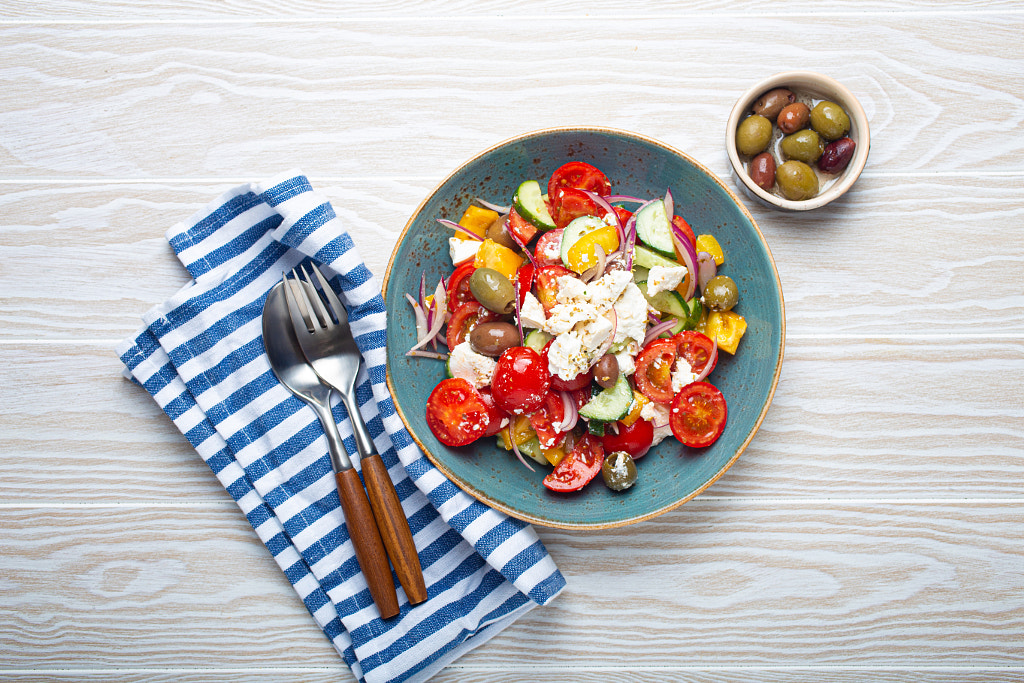 Greek salad with feta cheese, vegetables, olives in blue bowl on white ...