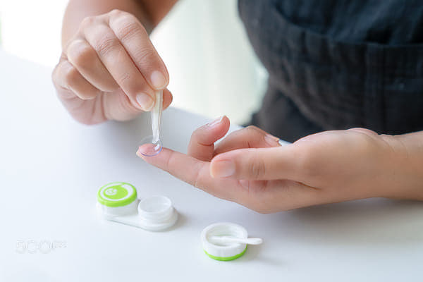 Girl puts contact lens on her index finger with tweezers. Close-up ...