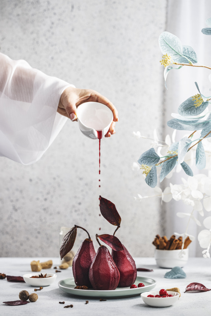 Women hand is pouring wine from small jar to plate with pears stewed in ...