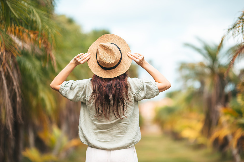 Back view of woman in straw hat outdoors among the palmtrees by Dmitrii ...