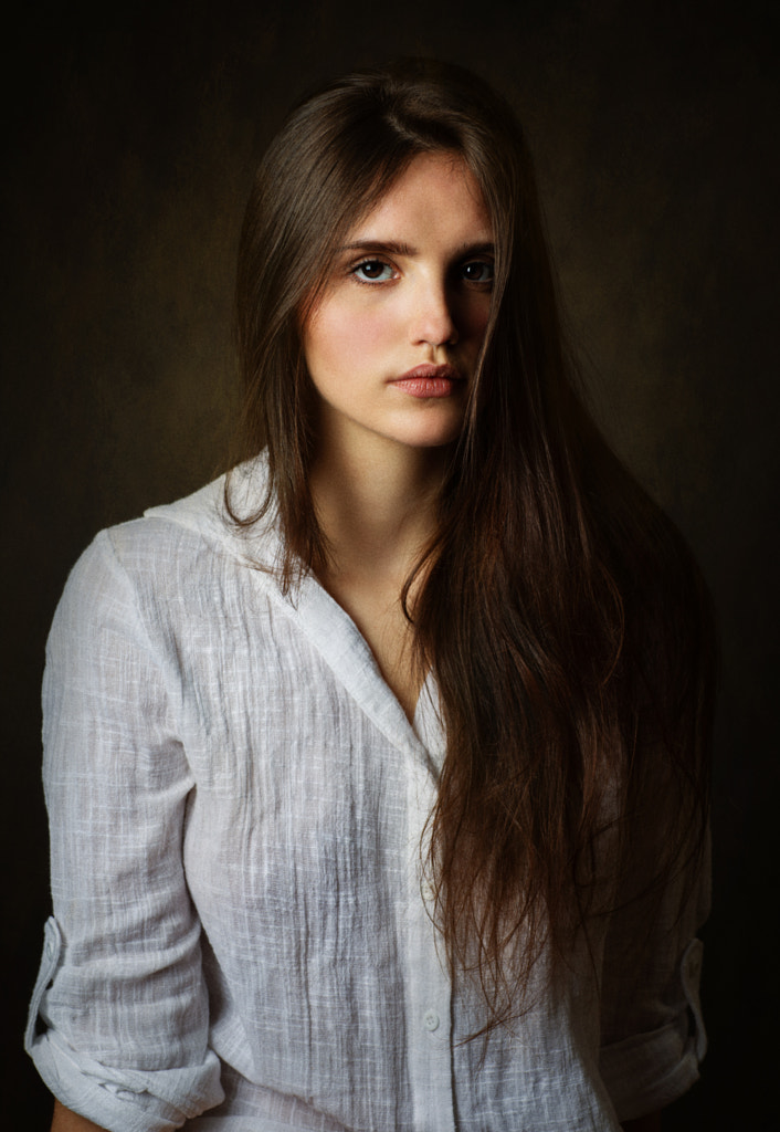 Portrait of young woman standing against black background by Zachar ...