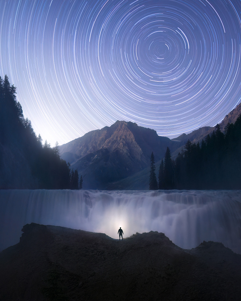 Star swirls with person standing in front at night by Alan Poelman / 500px