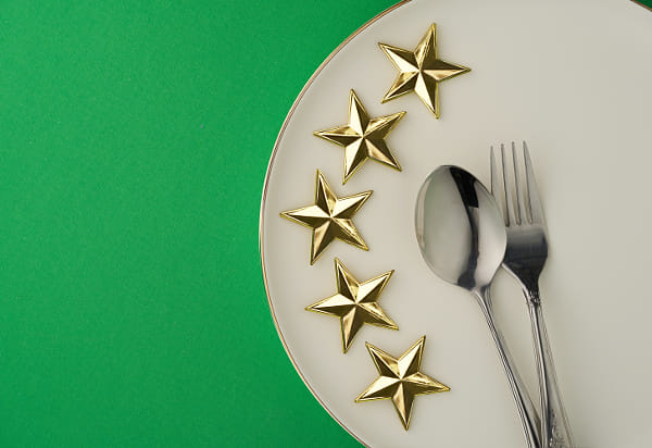 Five gold star on white plate with fork and spoon on green background ...