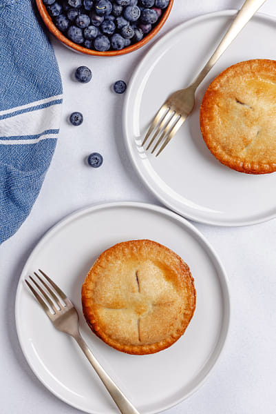 Two mini blueberry pies on the white plates, overhead view by Diana ...