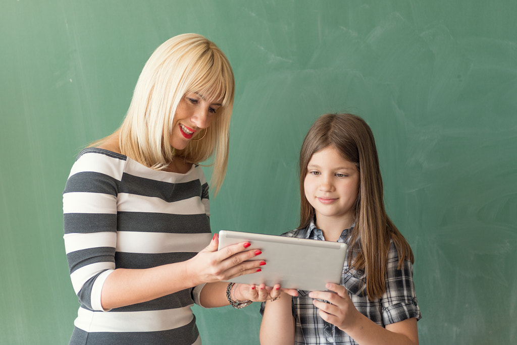 Teacher and primary school student using tablet by Igor Milic / 500px