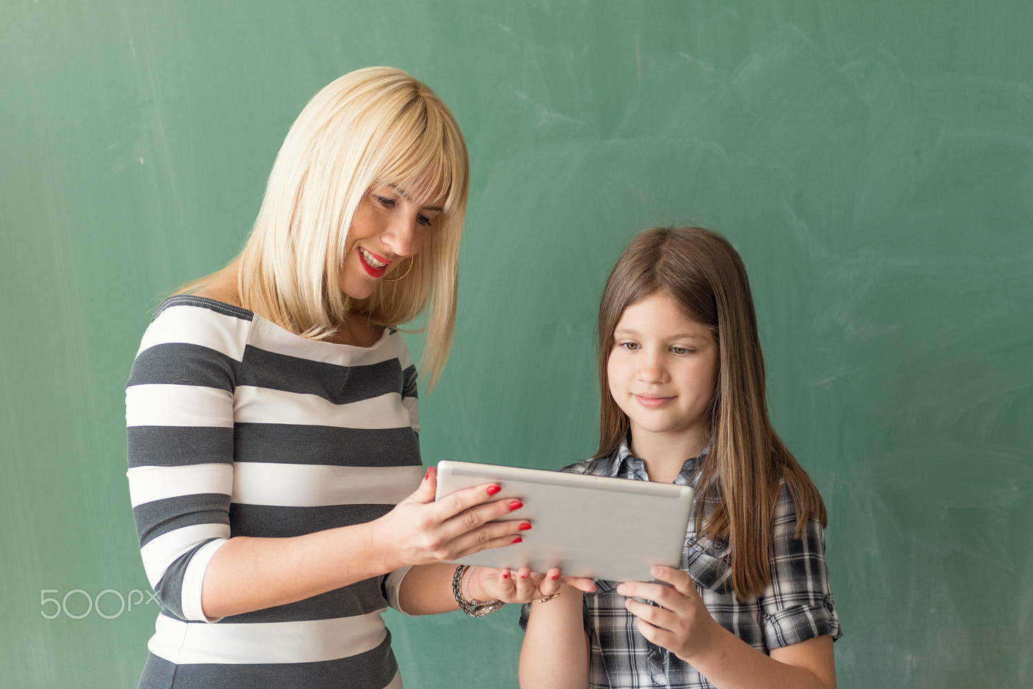 Teacher and primary school student using tablet by Igor Milic / 500px