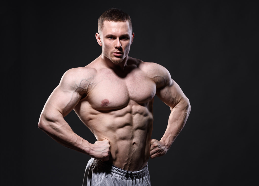 Strong muscular man posing in studio over dark background by Oleg Evseev / 500px