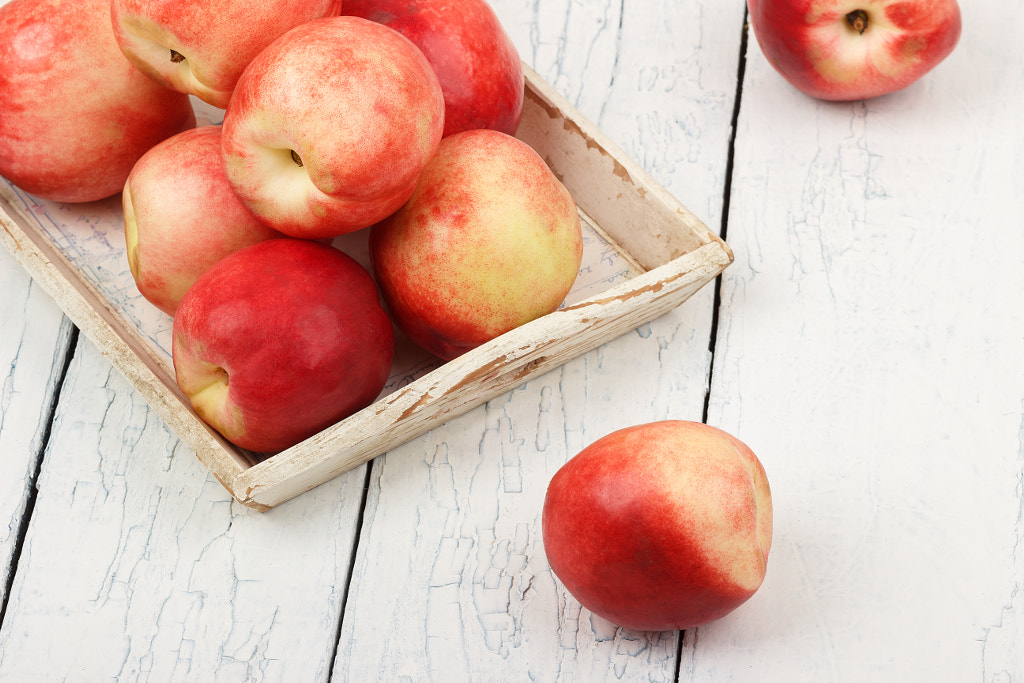 Ripe red peaches in the tray on the white wooden table by Елизавета ...