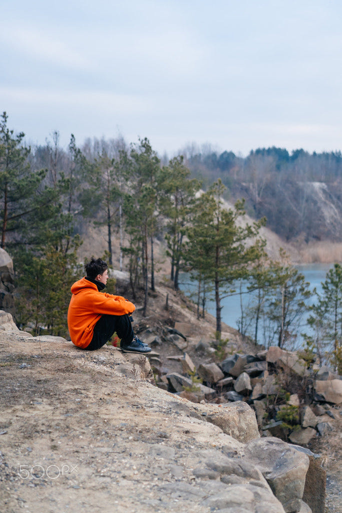 A young man sitting on the edge of a cliff poses for the camera by ...