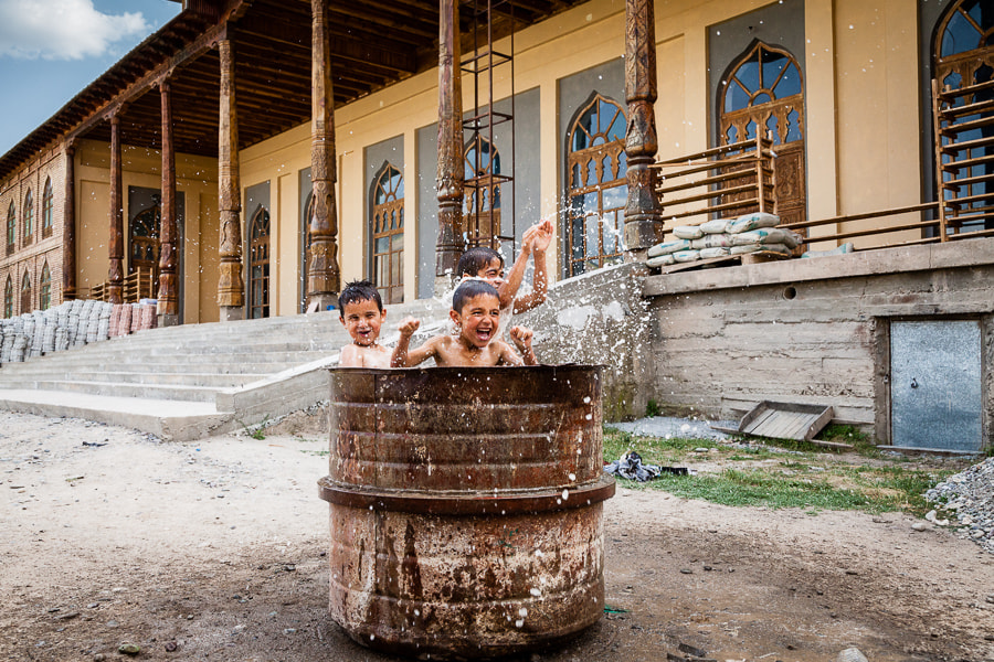 Tajik children playing in drum of water outside mosque by Damon Lynch ...